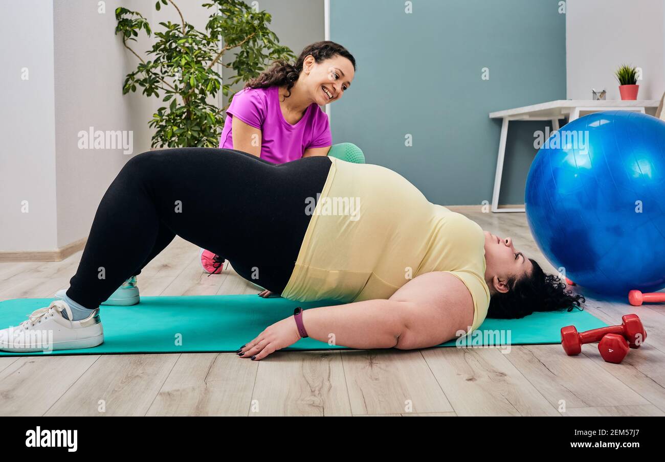 Overweight woman exercising lying on a yoga mat, personal trainer ...