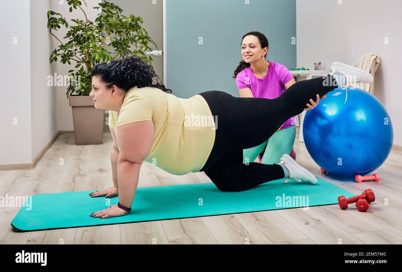 Personal female trainer helping overweight woman do leg muscle ...