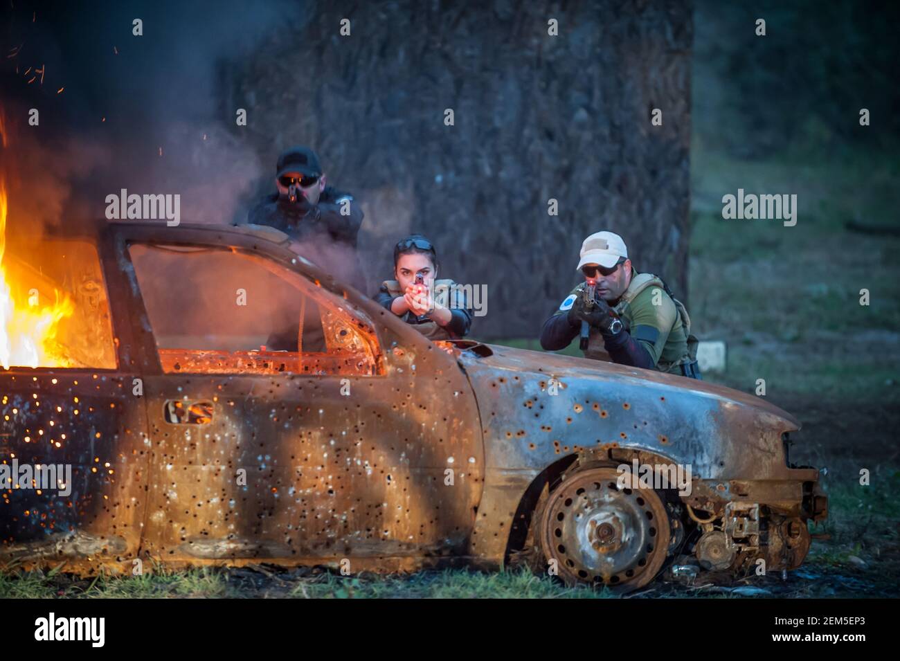 Army soldier hiding behind burning car shooting from machine gun ...