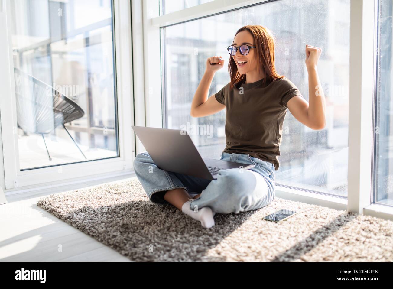 Young woman using computer laptop sitting on the floor celebrating mad ...