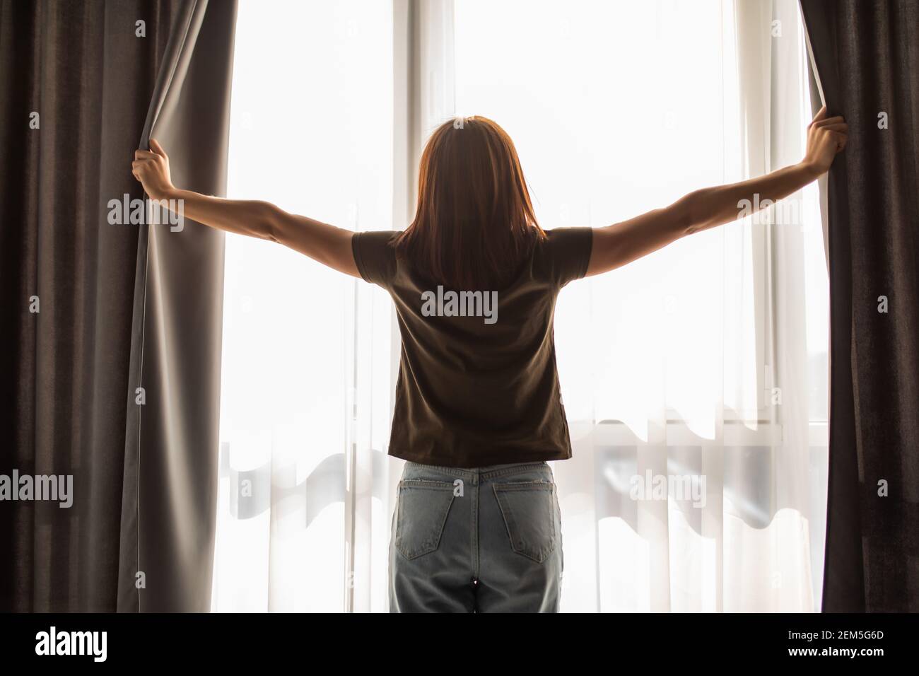 Beautiful woman opening curtains and looking through the window Stock ...