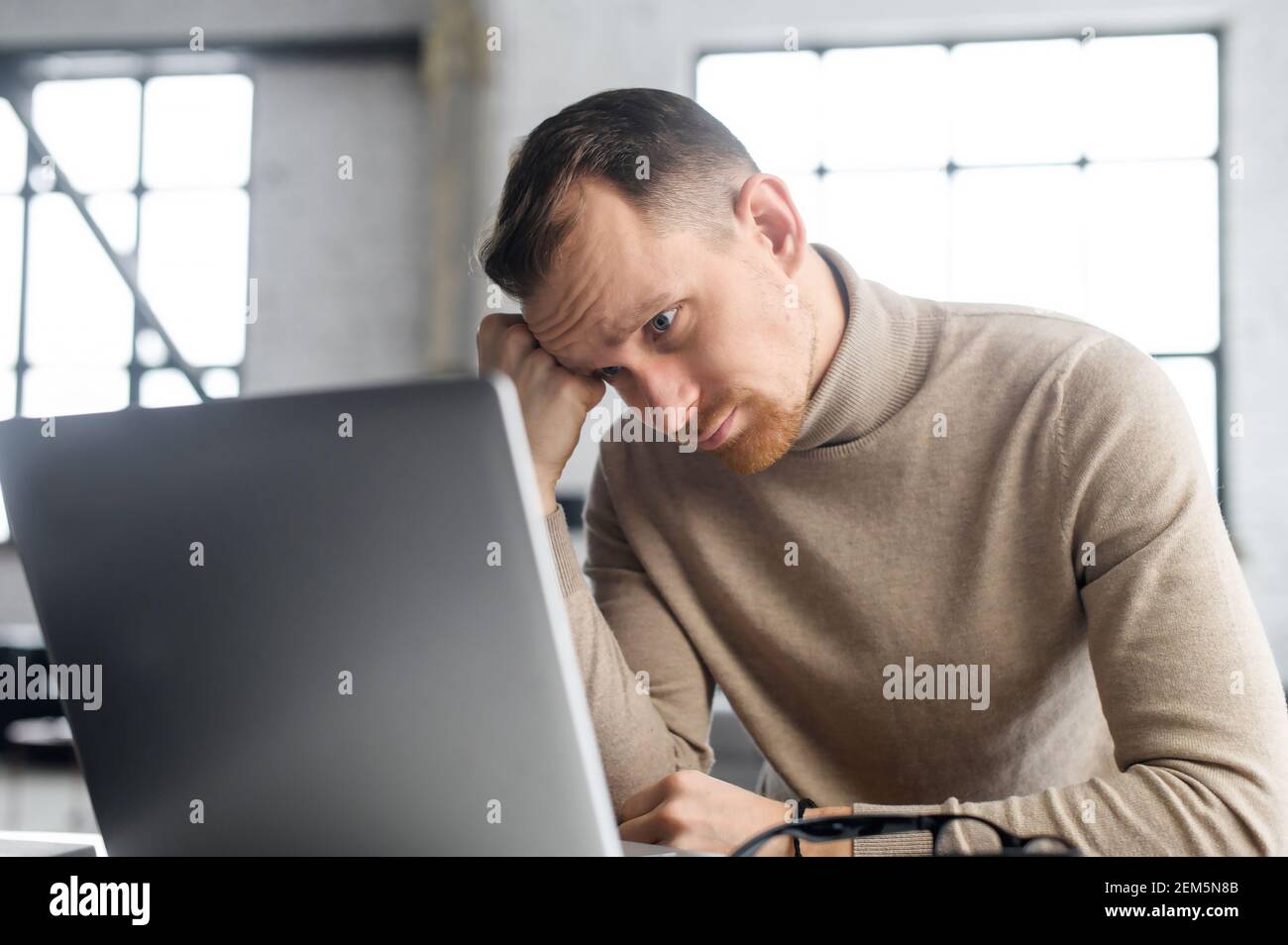 Young disappointed businessman sitting at the laptop, propped his head ...