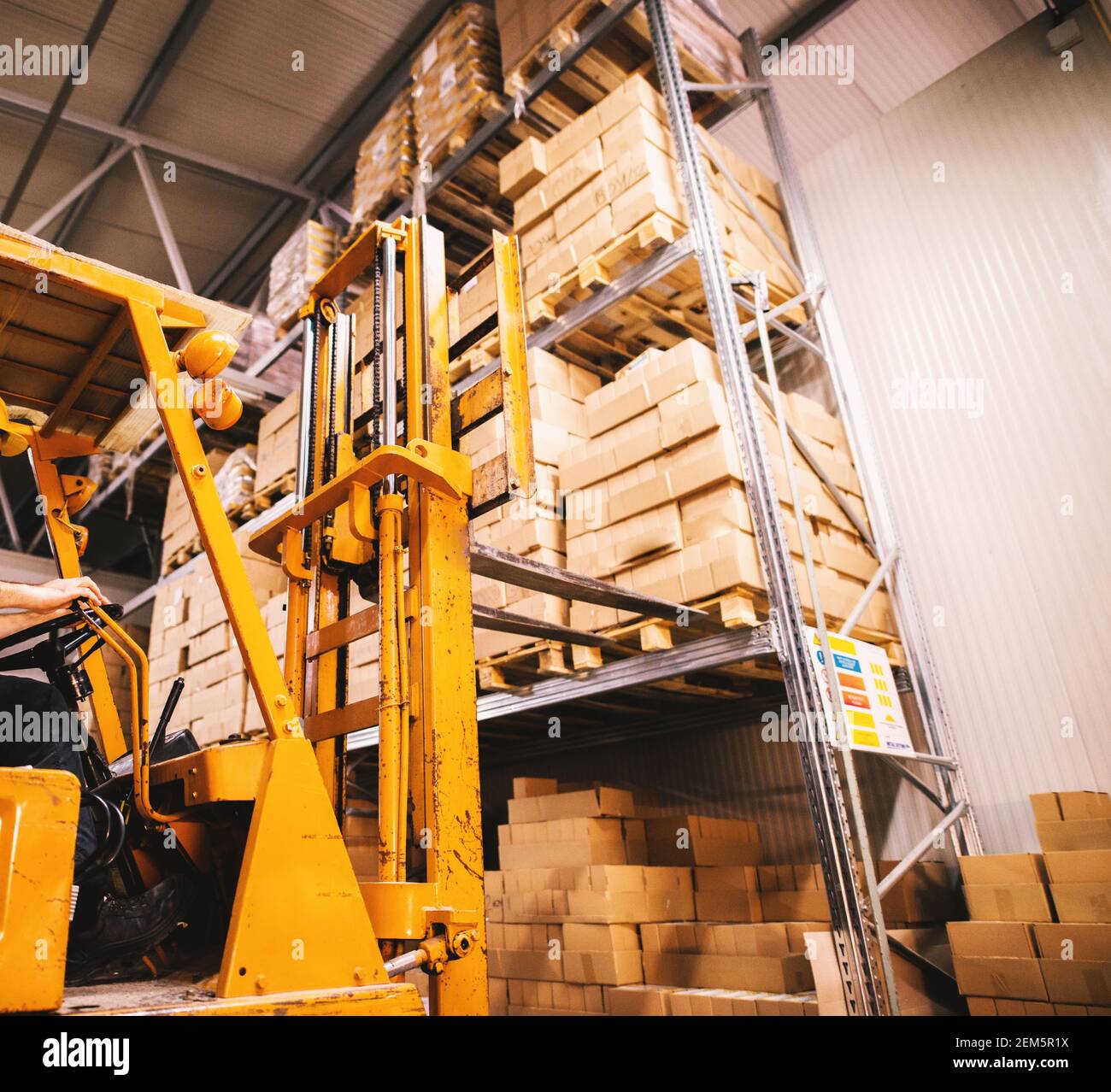 Fork lifter approaching pallet filled with stacks of boxes on a rack in ...