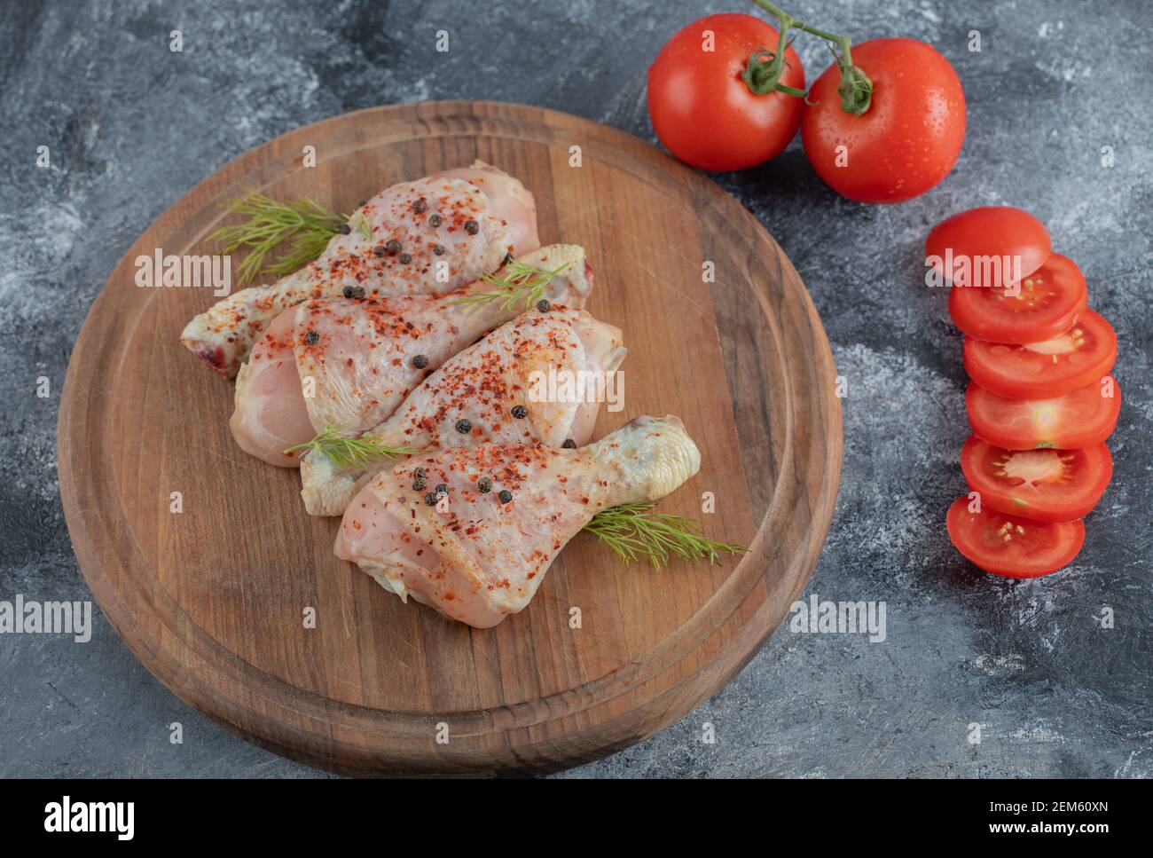 Raw chicken legs with spices and sliced or whole tomatoes on a wooden ...