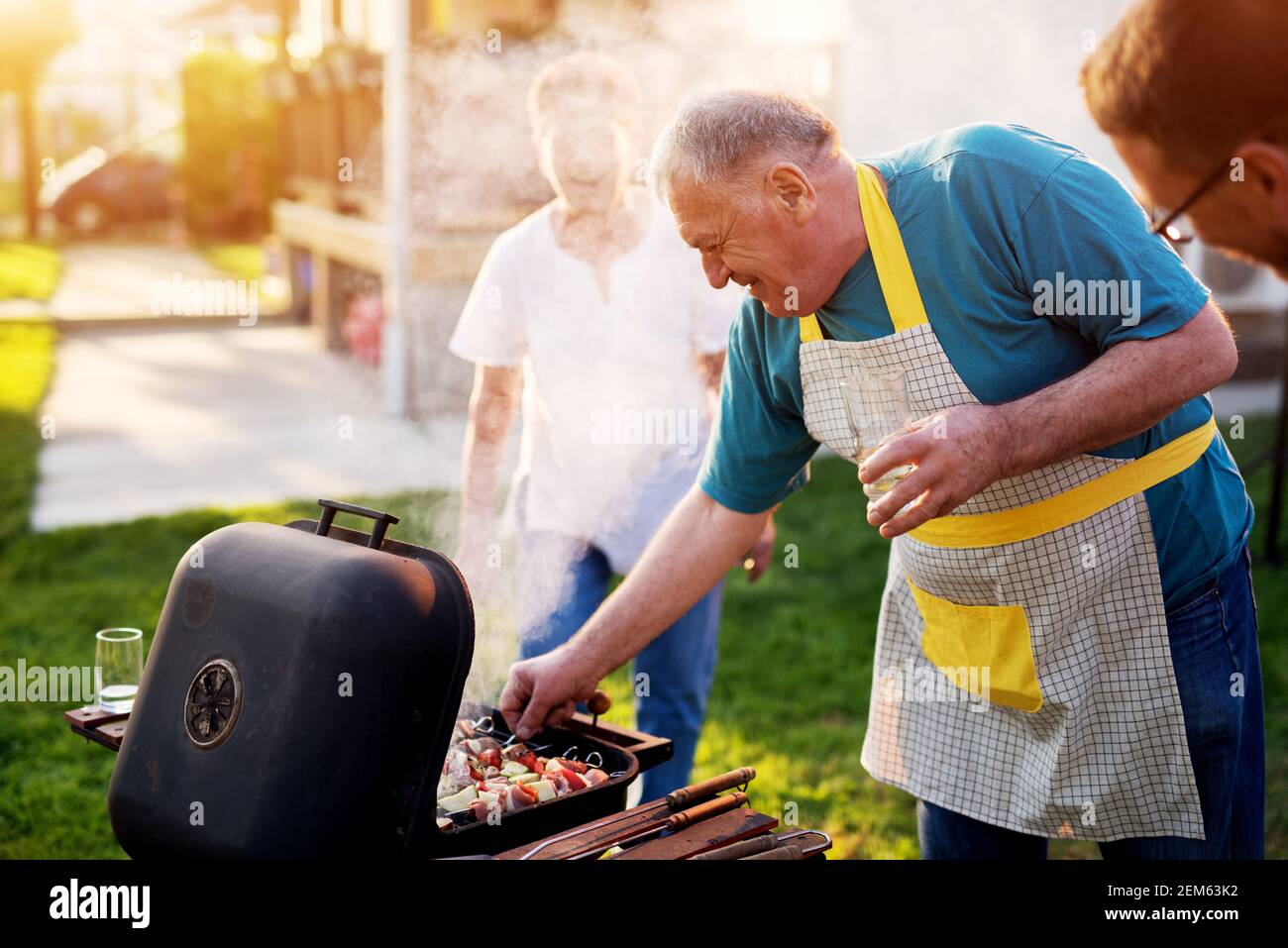 Elderly man is carefully inspecting should he take meat off the grill ...