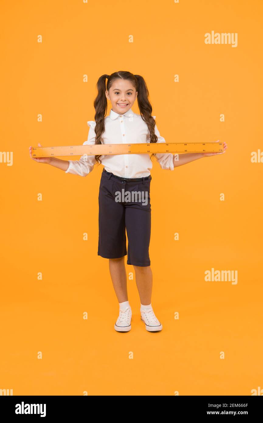 Measuring length. Little girl holding metric ruler on yellow background ...