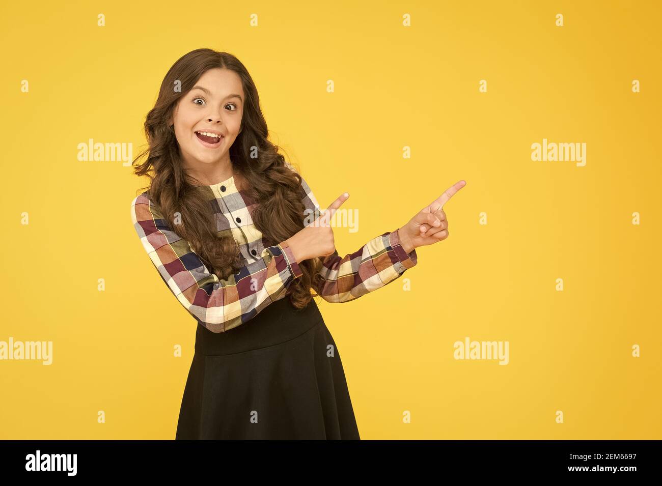 Check it out. Happy girl pointing at yellow background copy space ...