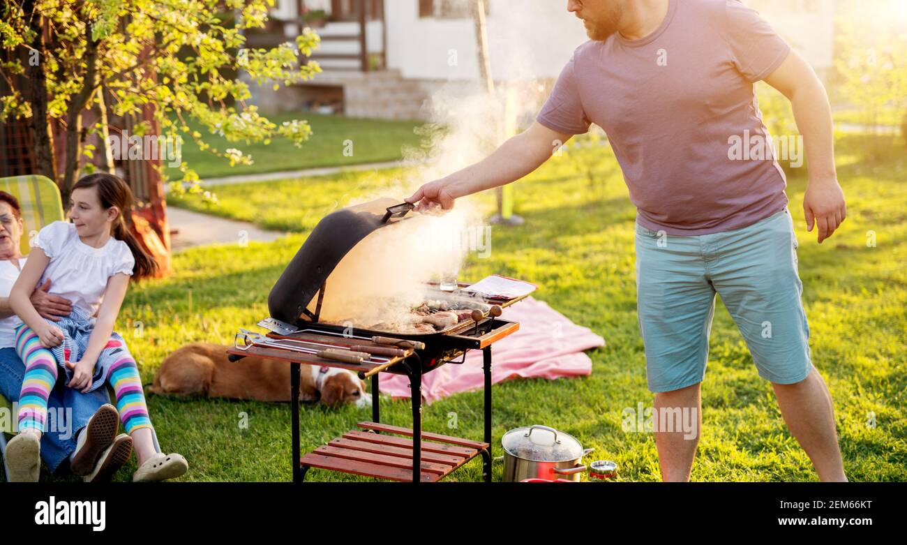 Man is opening grill cap releasing all the steam and arom of meat being ...