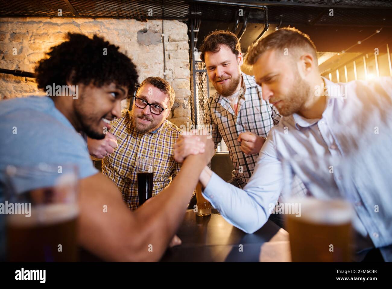 Happy mixed-race male friends having arm wrestling challenge at the ...