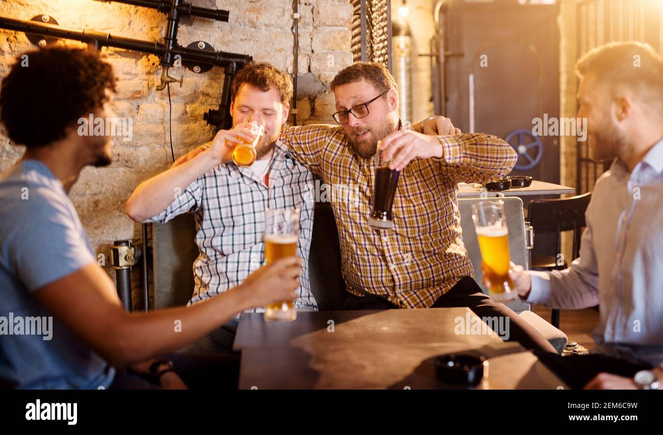 Drunk satisfied multicultural male friends raising a draft beer and ...