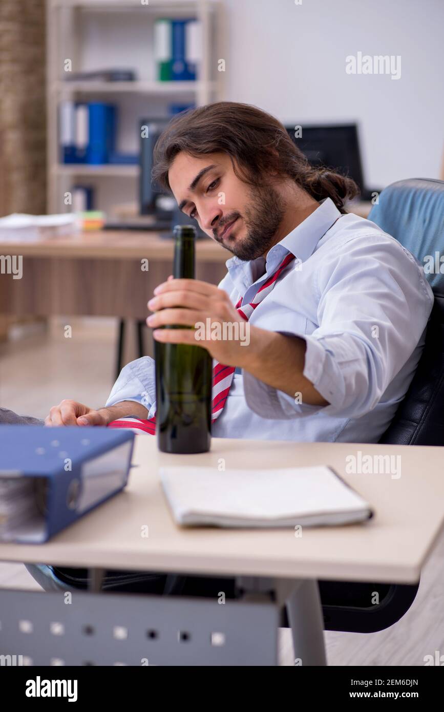 Young male employee drinking alcohol at workplace Stock Photo - Alamy