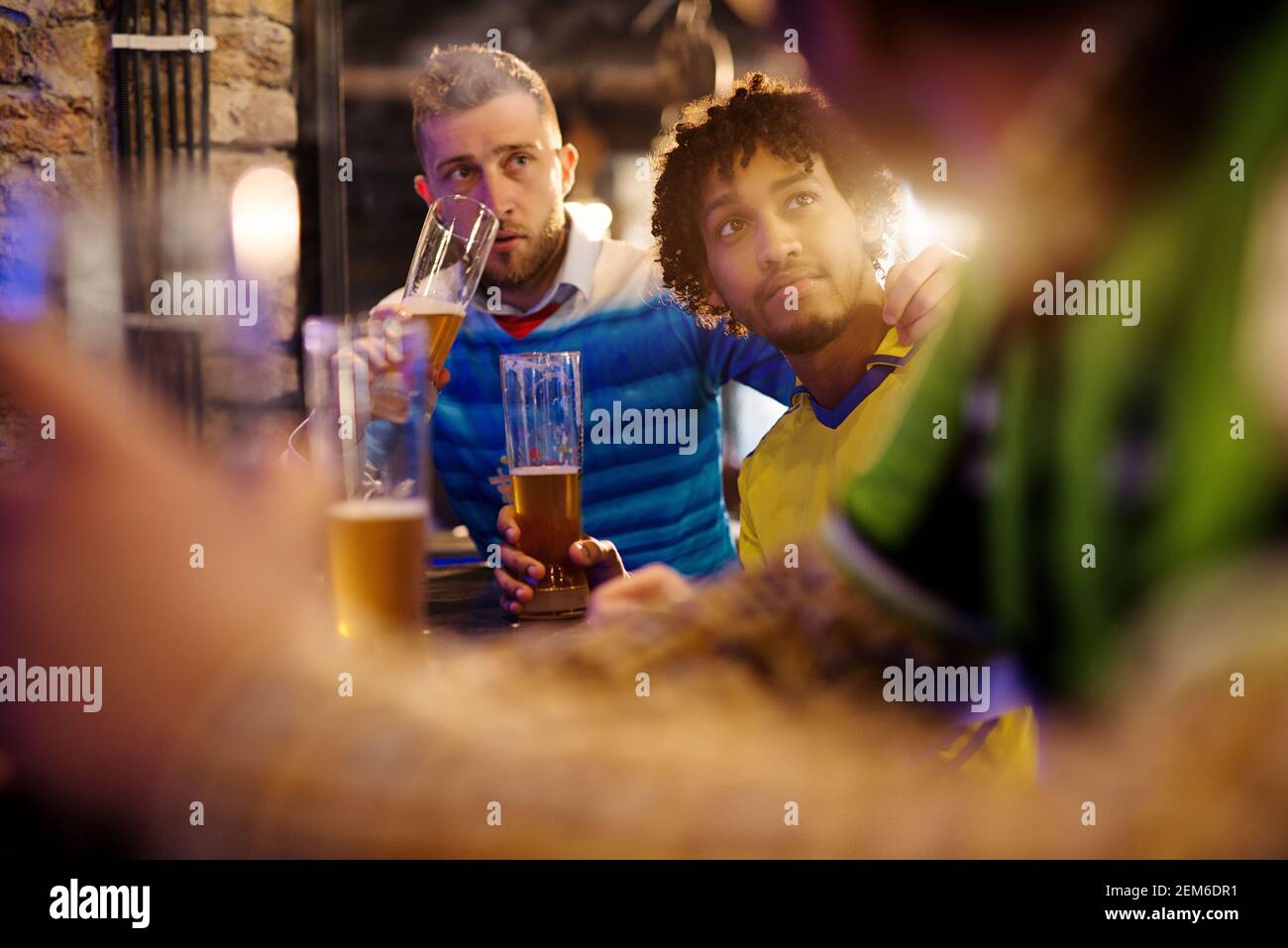 Group of diverse soccer fans met in a pub and are having a beer while ...