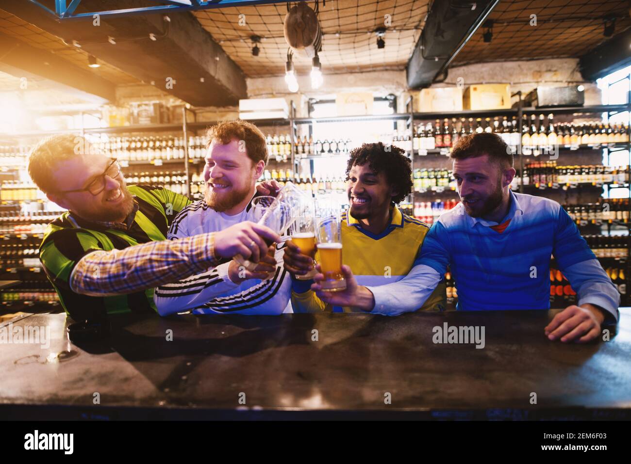Joyful football fans are sitting by the counter and leaning their beers ...