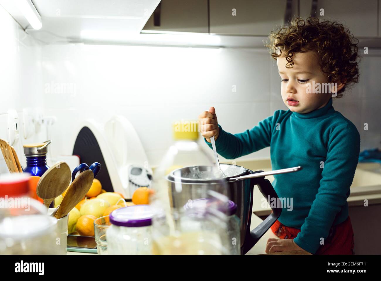 Little curly-haired girl plays cooking in a real kitchen with natural ...