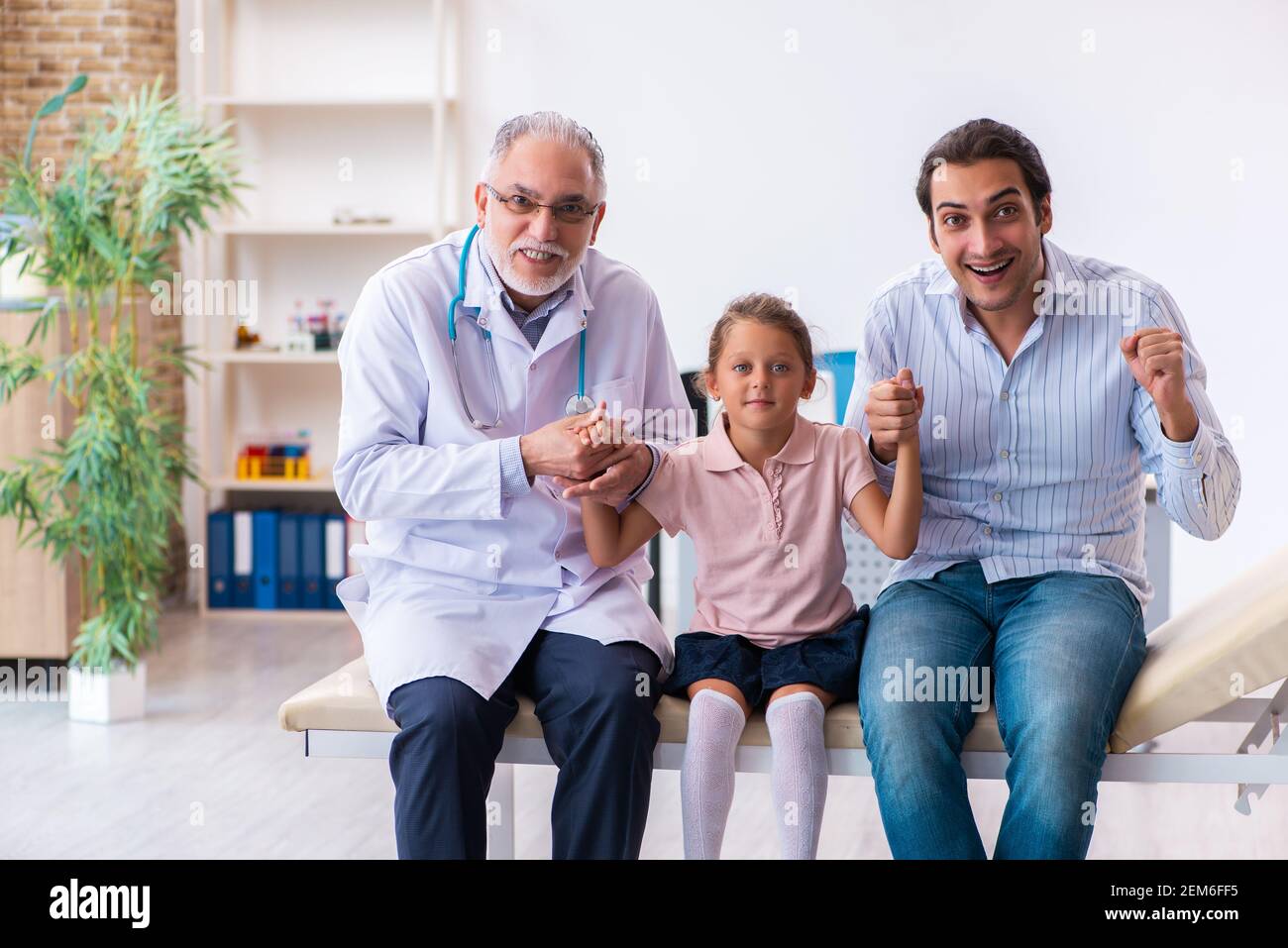 Little girl with her father visiting old male doctor Stock Photo - Alamy