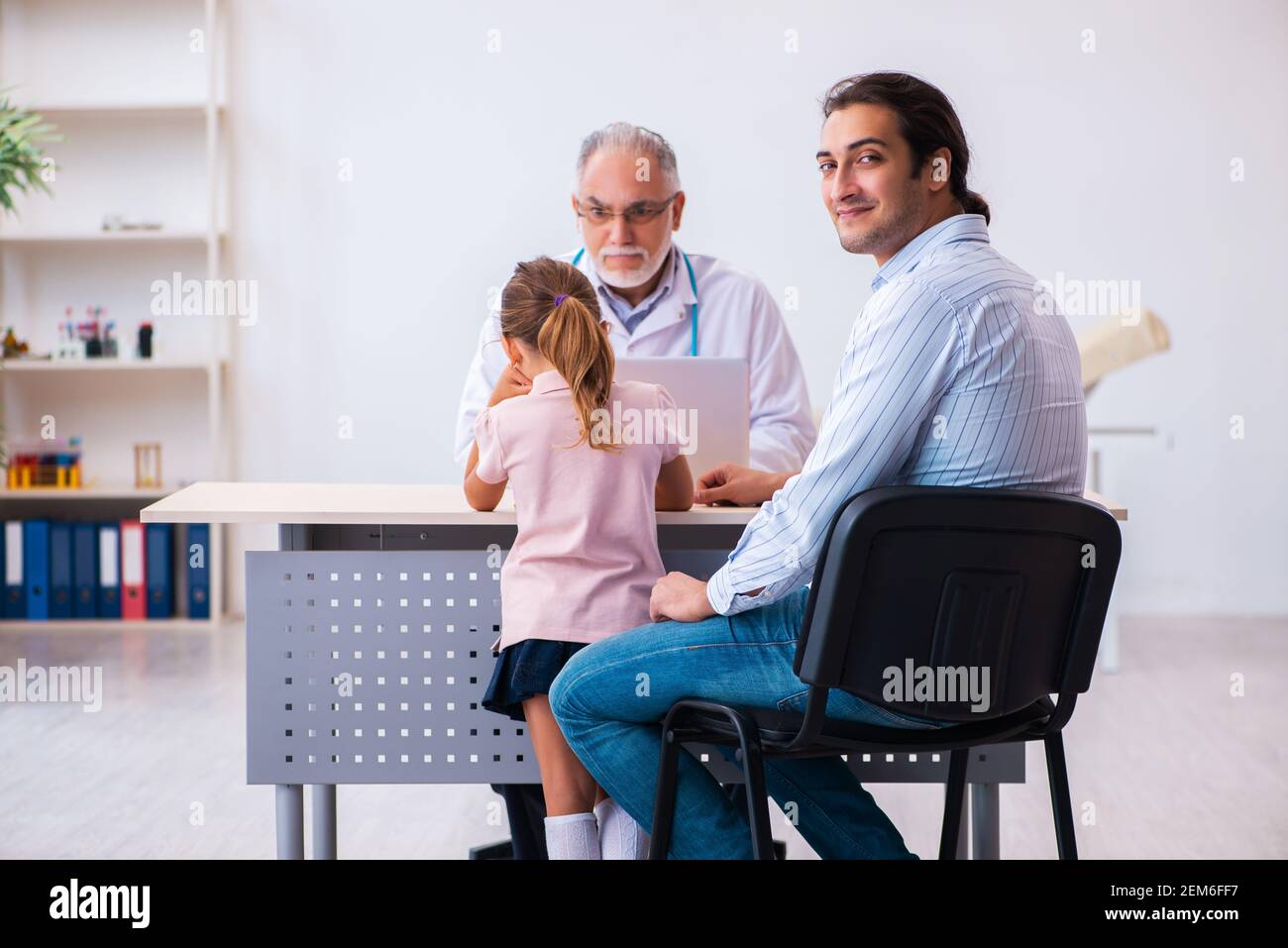 Little girl with her father visiting old male doctor Stock Photo - Alamy
