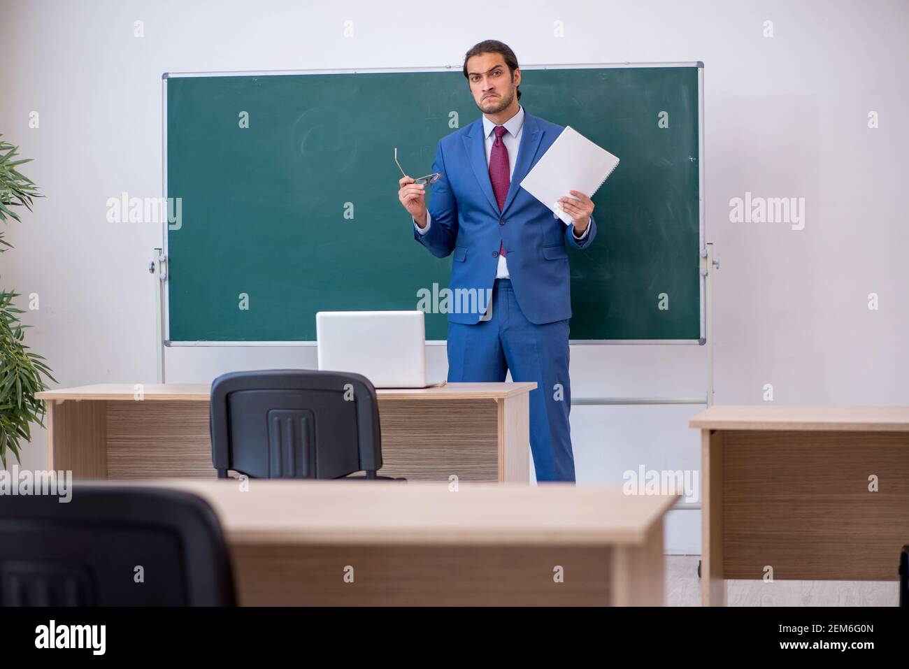 Young teacher in suit in front of green board Stock Photo - Alamy