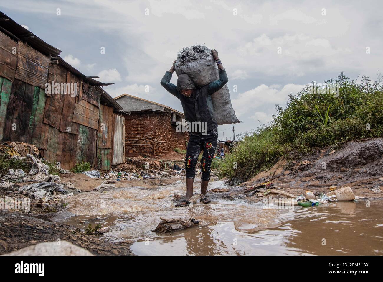 A man carrying a heavy sack of Charcoal crosses a local sewer river in ...