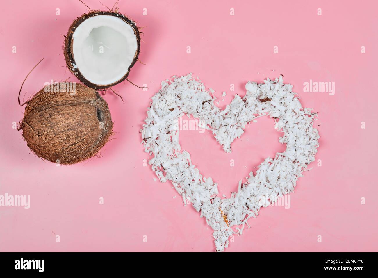 Coconut halves and coconut pieces shaped like heart on pink background ...