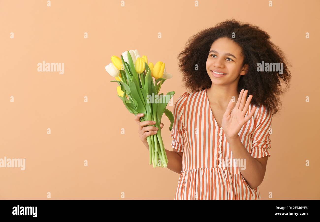Teenage African-American girl with spring flowers on color background ...
