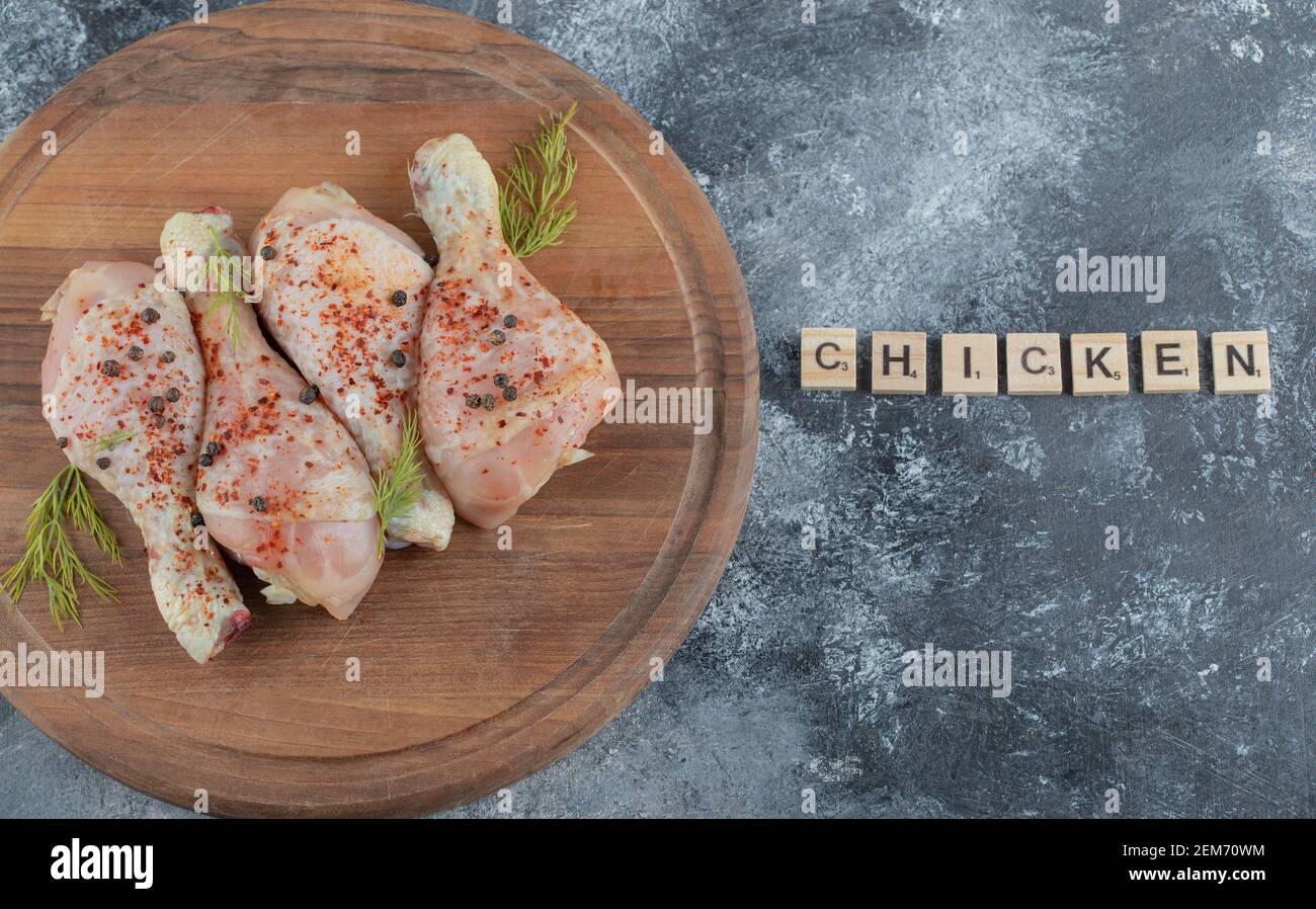 Top view of marinated raw chicken legs on wooden board over grey ...