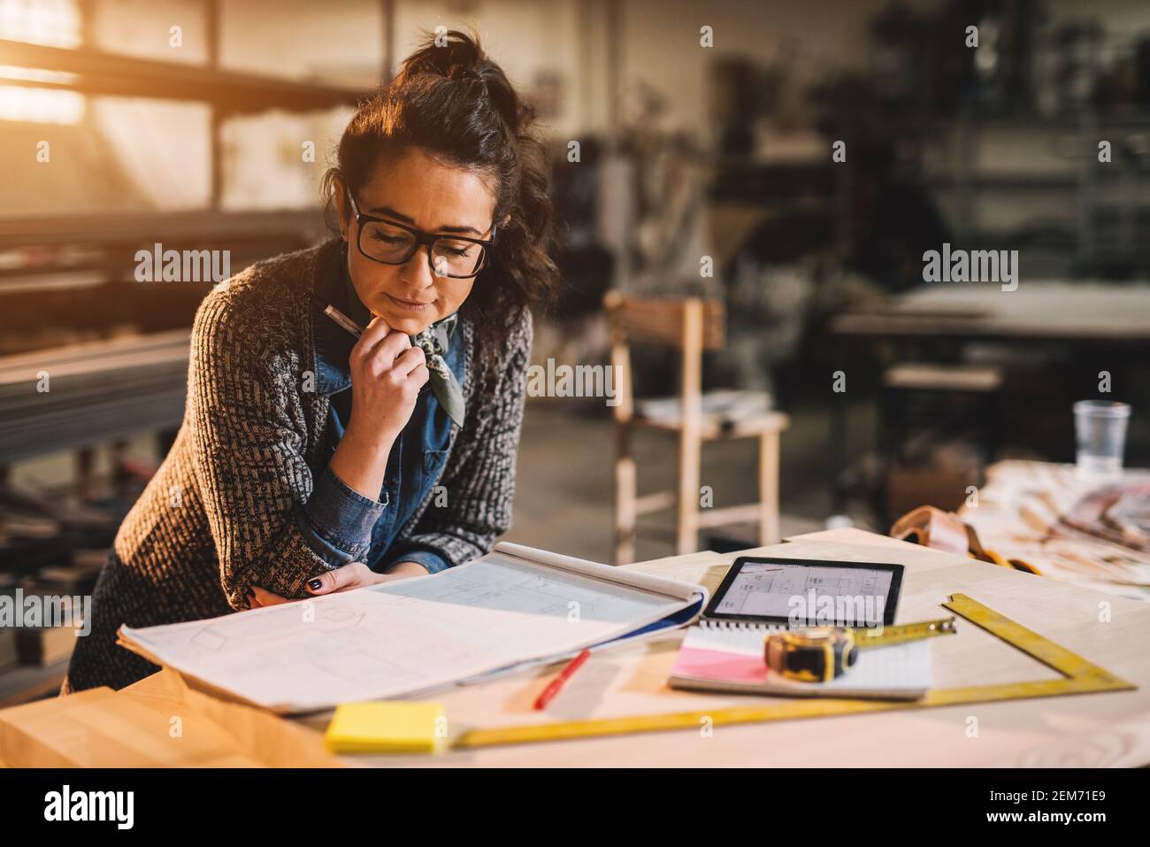 Thoughtful beautiful middle-aged female engineer looking at blueprints ...
