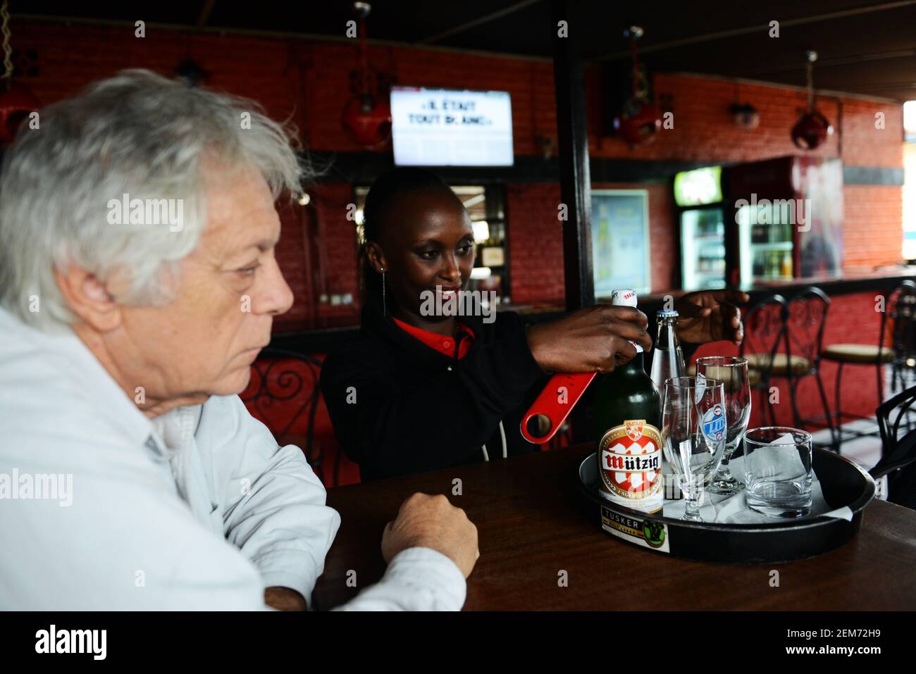 A Rwandan woman pouring Mützig beer into a glass in a pub in Kigali ...