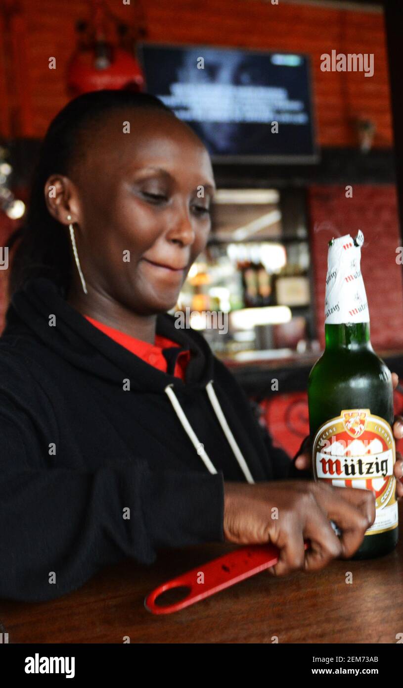 A Rwandan woman pouring Mützig beer into a glass in a pub in Kigali ...
