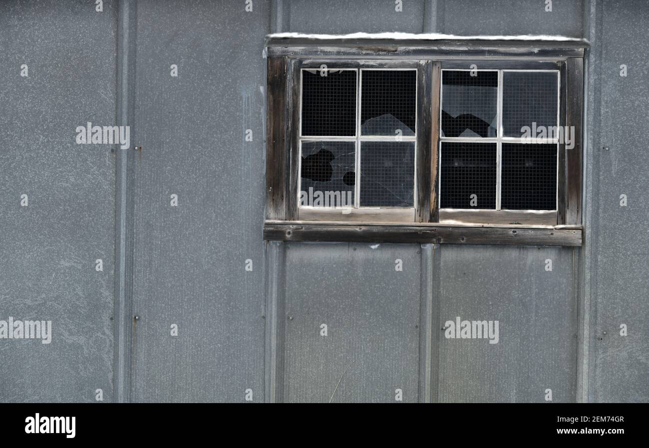Broken windows with a bit of snow on the window frame, in a grey, rural ...