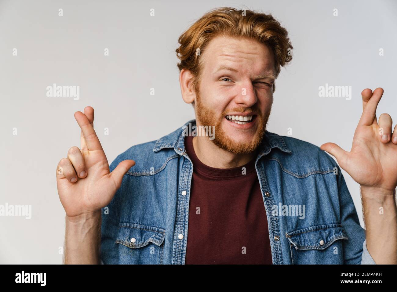Joyful redhead guy winking while posing with fingers crossed for good ...