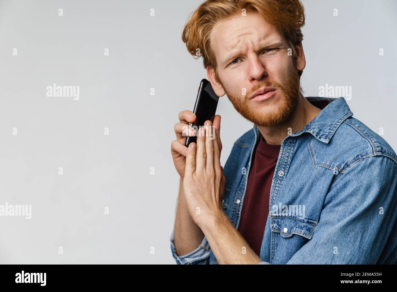 Confused redhead guy looking at camera and using cellphone isolated ...