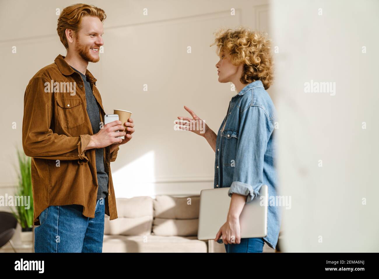 Two cheerful young people holding coffee cups and talking while ...