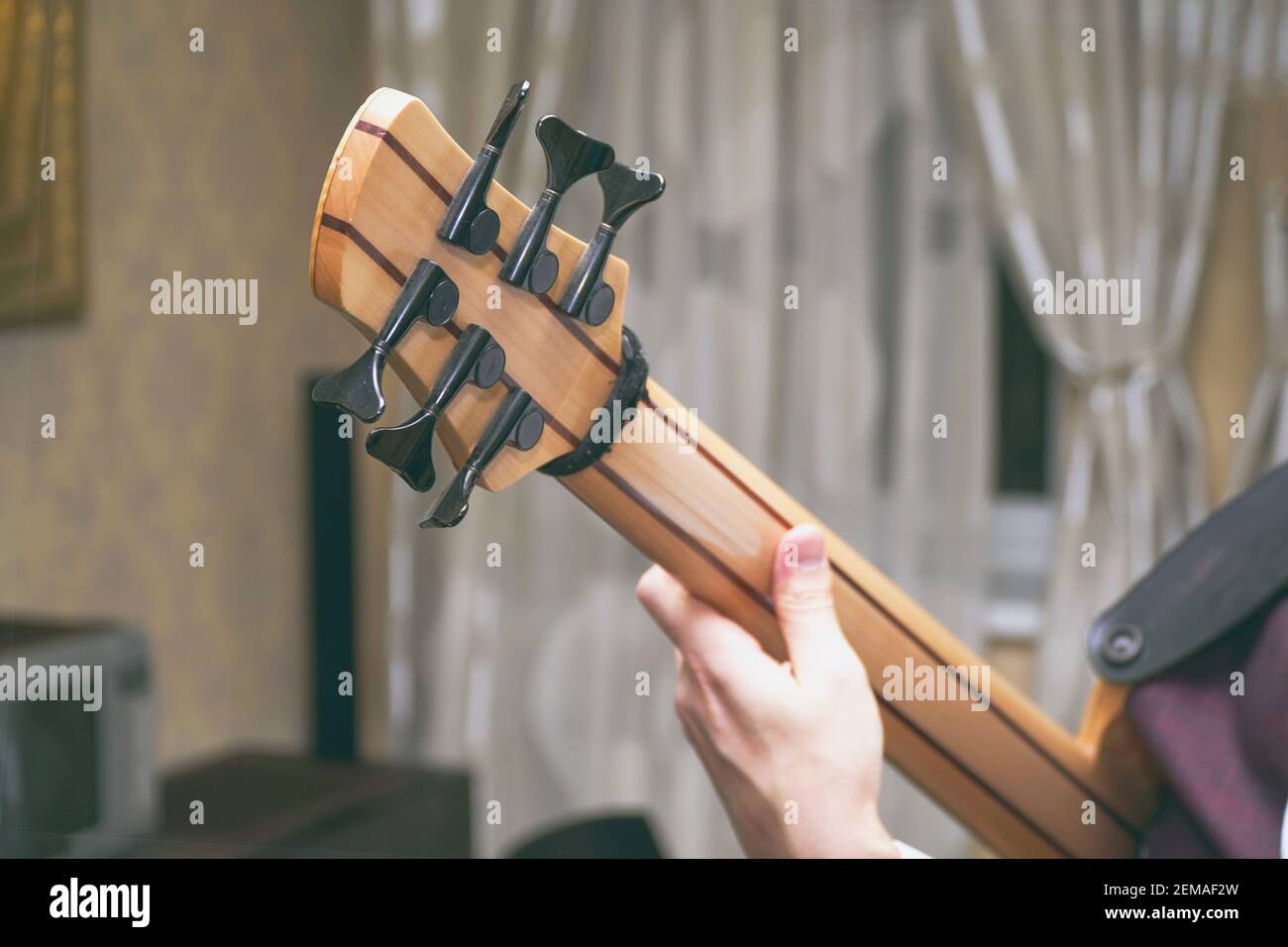 The guitarist's hand on the neck of a six-string bass guitar. Rear view ...