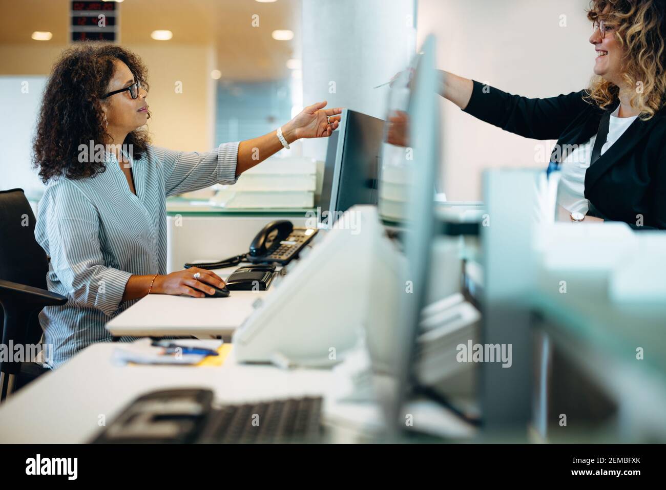 Woman standing at reception desk giving her card to the receptionist ...