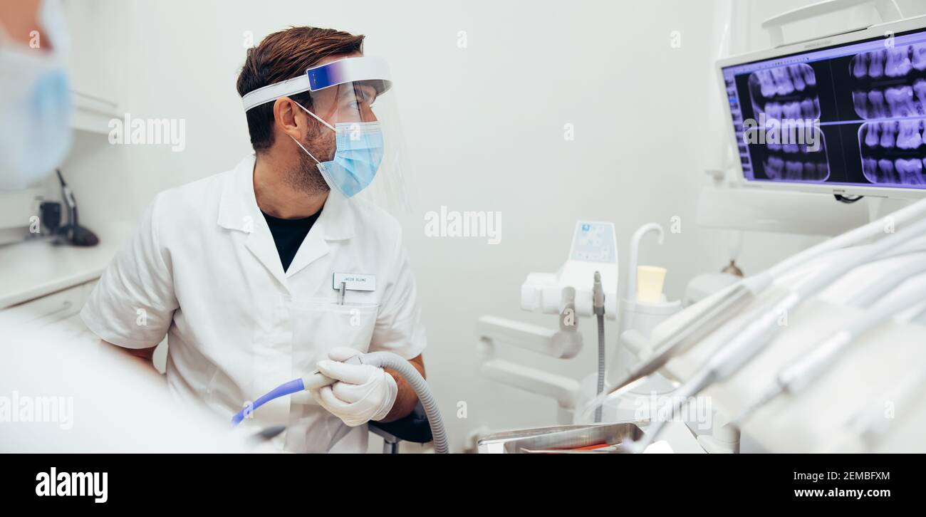 Doctor wearing protective face shield and face mask looking at x-ray ...