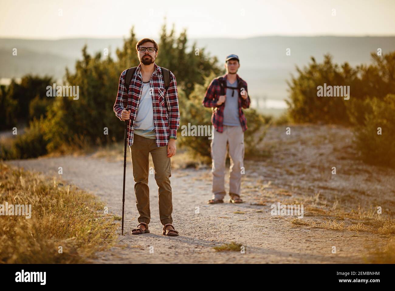two men hikers enjoy a walk in nature, sunset time in summer. enjoying their adventure ...