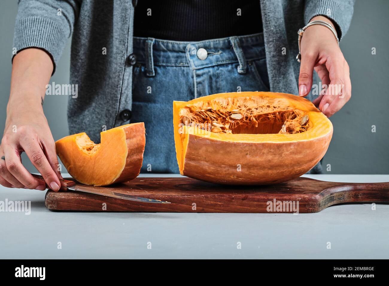 A woman hand cutting a slice of pumpkin with knife on the wooden board ...