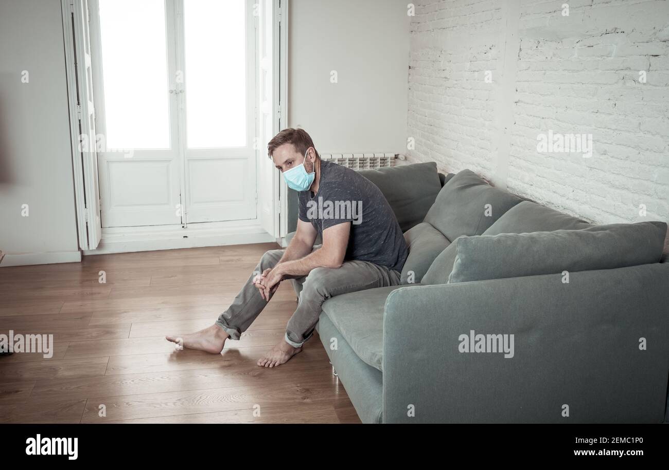 Sad man with protective face mask at home living room couch feeling ...