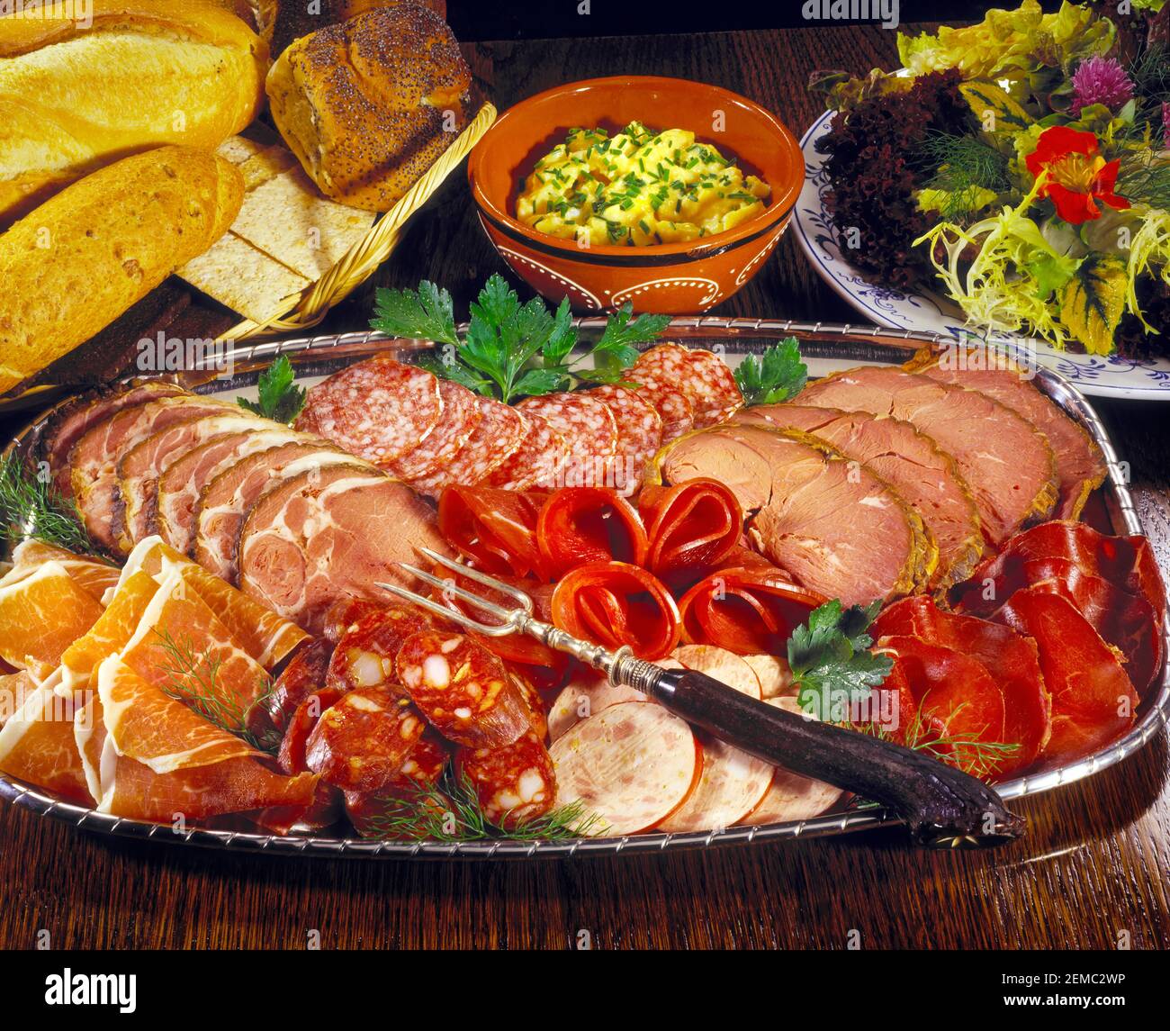 Cold meat platter with bread and salad, on silver plate on dark wooden ...