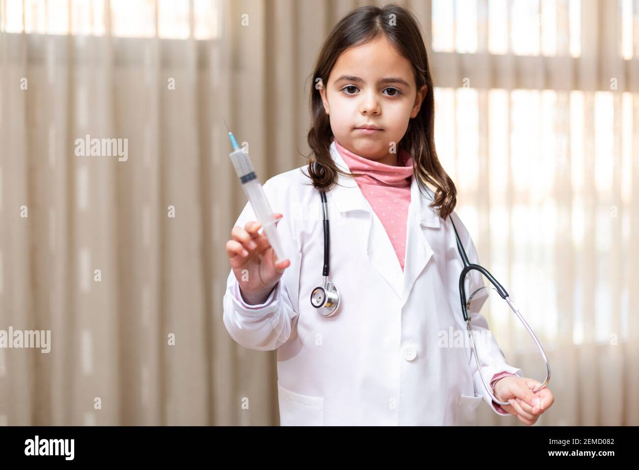 Little girl in doctor's uniform holding a syringe in her hand. Concept ...