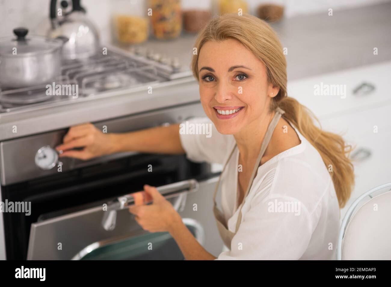 Blonde woman opening the oven in the kitchen while cooking dinner Stock ...