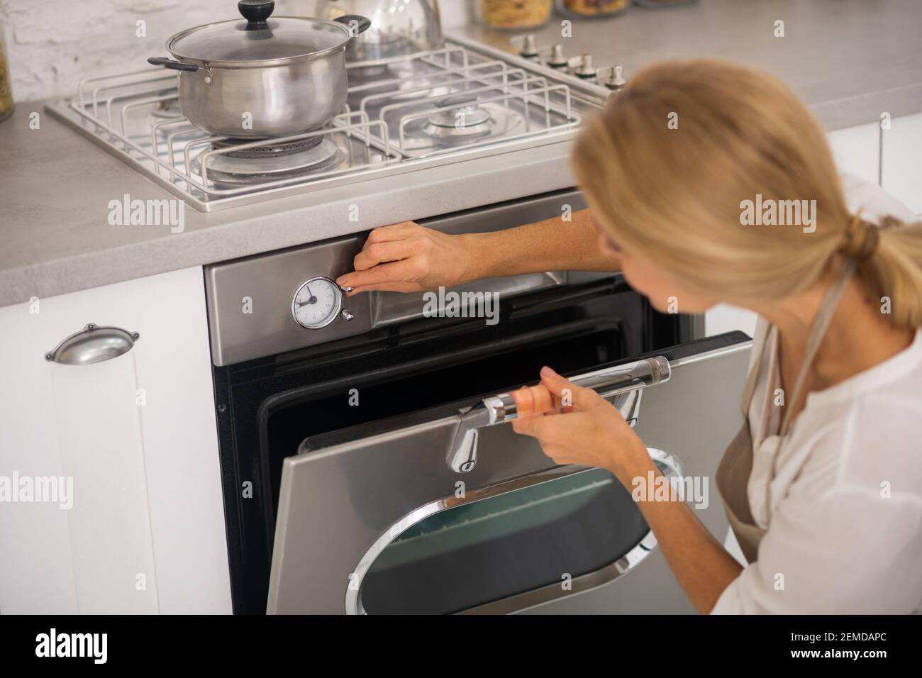 Blonde woman opening the oven in the kitchen while cooking dinner Stock ...