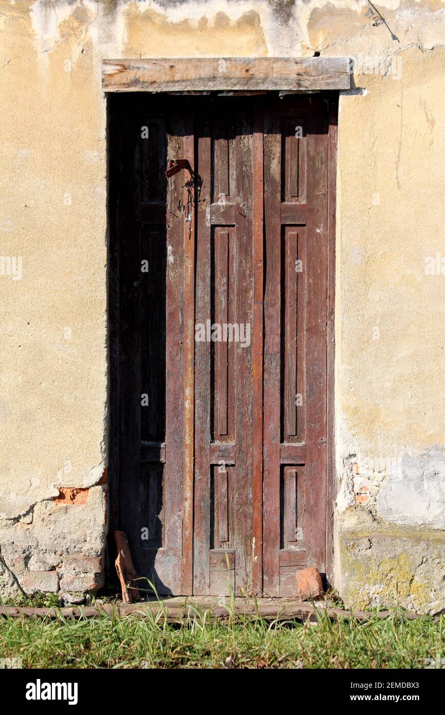 Dilapidated old wooden entrance doors with rusted metal frame mounted on cracked light yellow ...