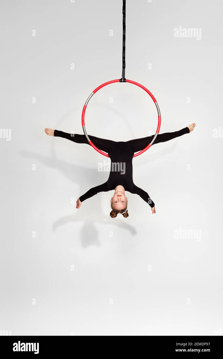 Little acrobat girl in black sportwear doing twine on an aerial hoop ...
