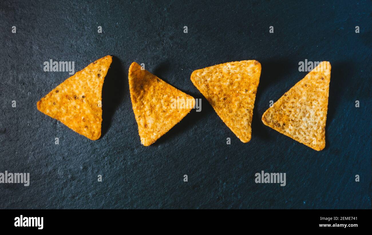 food background. Four Yellow triangle shaped tortilla chips on black ...