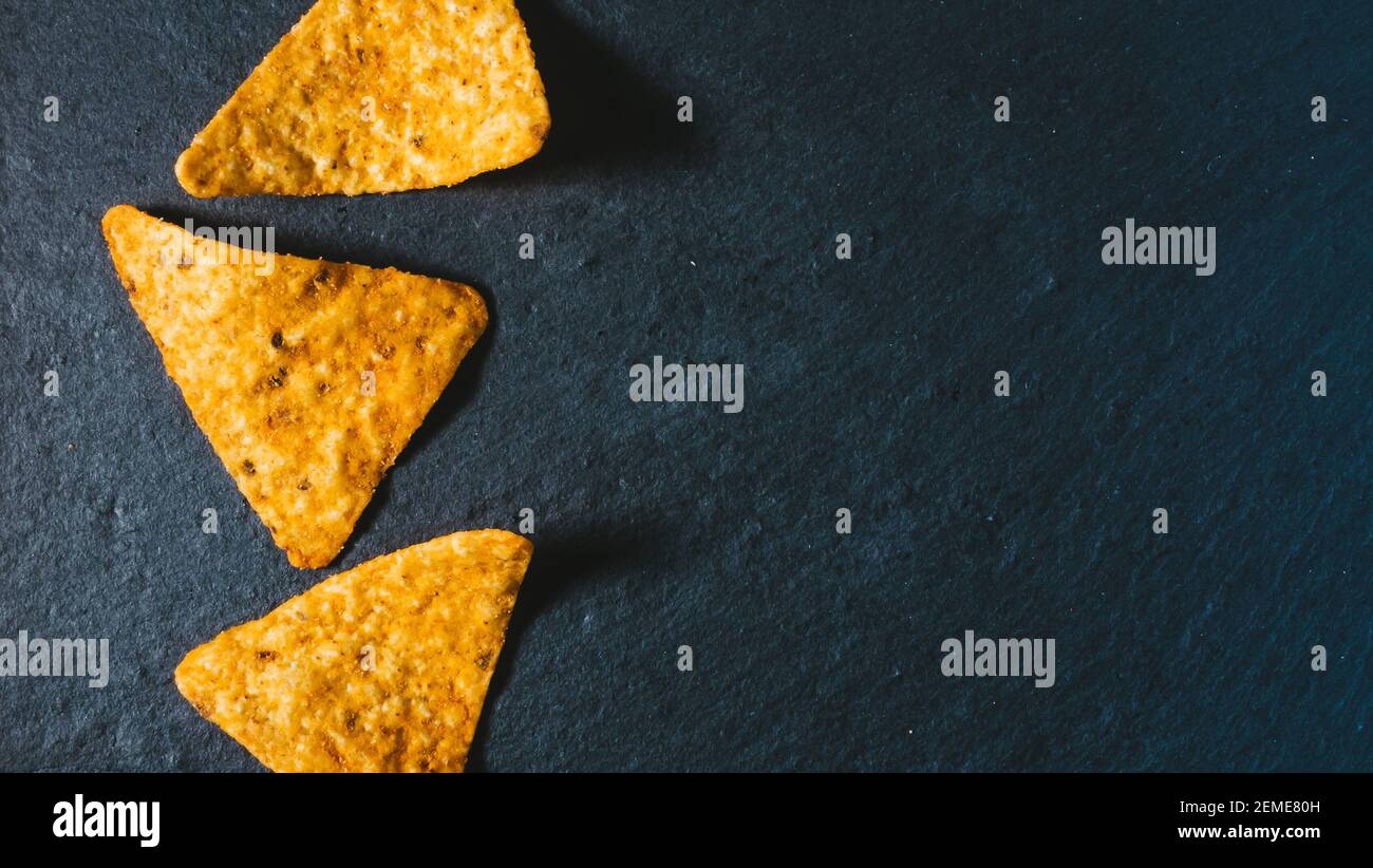 food background. three Yellow triangle shaped tortilla chips on black ...
