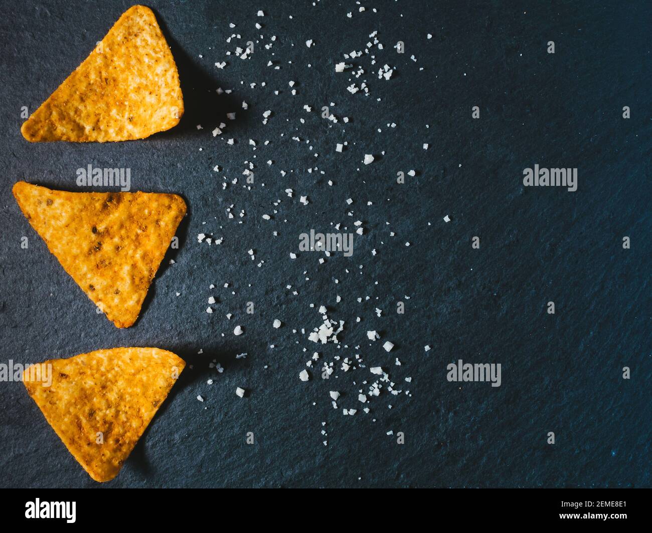 food background. three Yellow triangle shaped tortilla chips on black ...