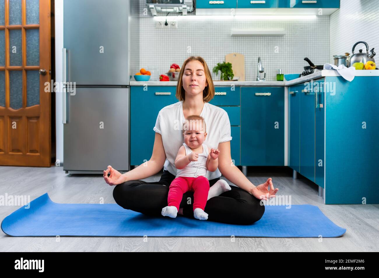 A young calm mother meditates in the kitchen while a nervous upset baby ...