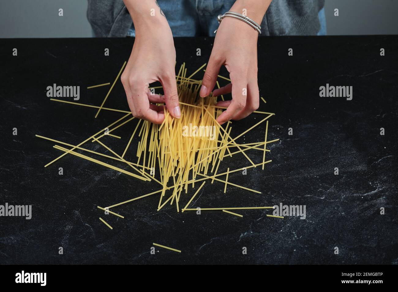 Woman holding raw spaghetti on dark table Stock Photo - Alamy