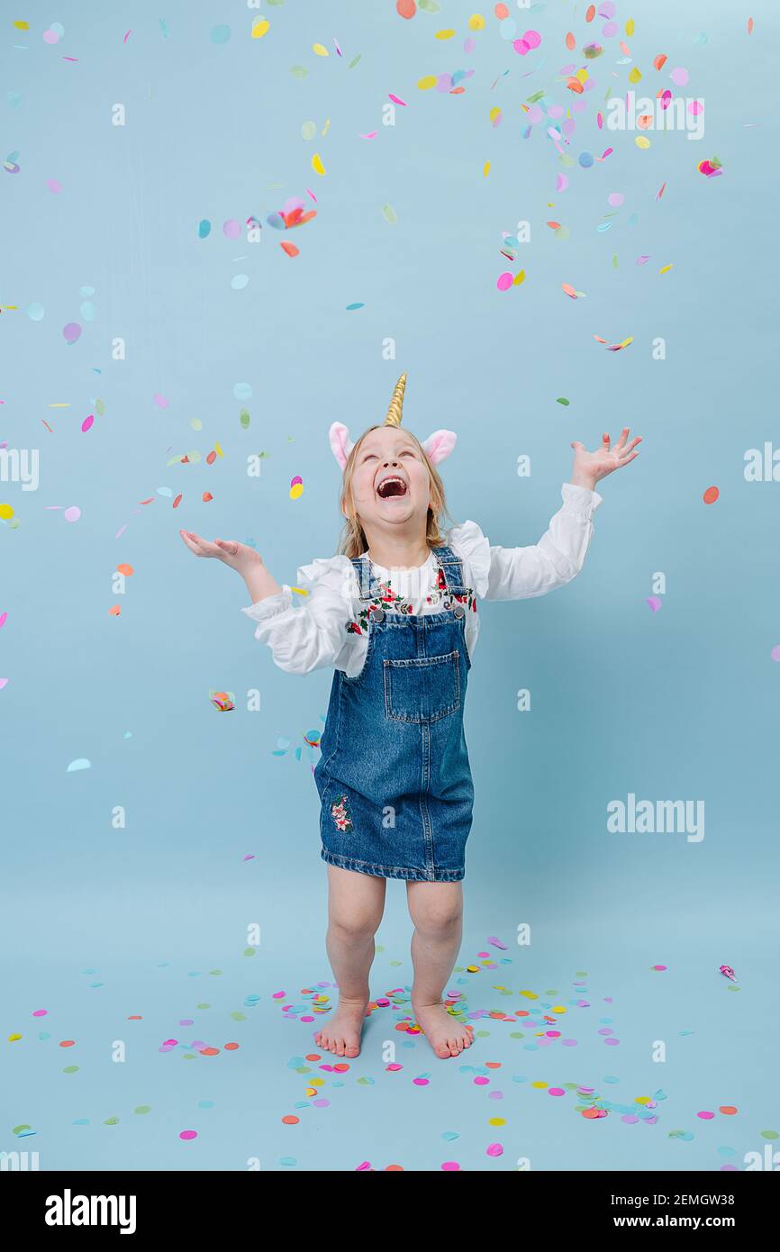Happy little girl in unicorn head band clapping her hands over blue ...